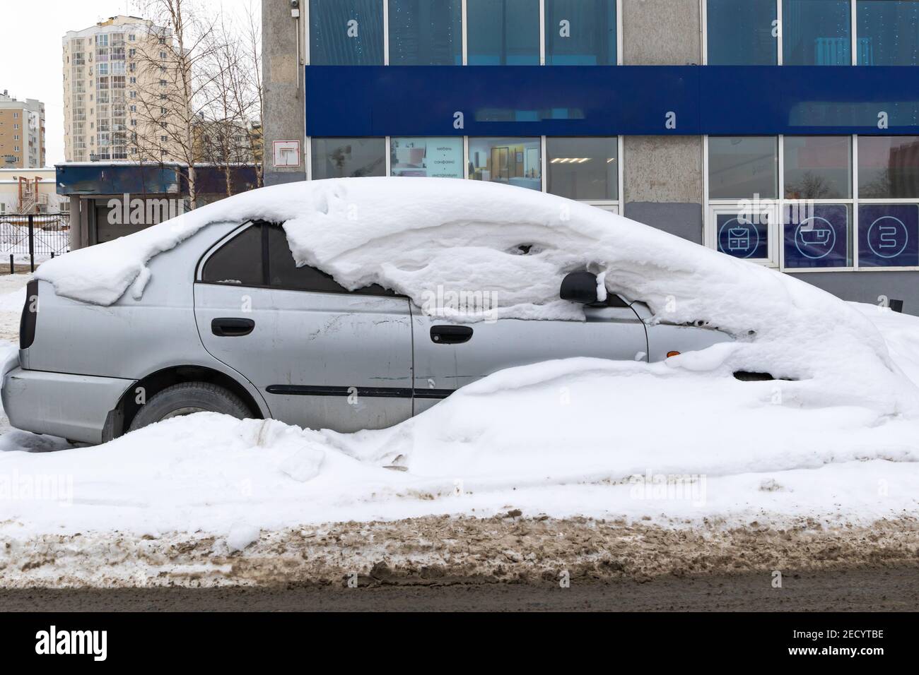 old abandoned broken car parked by the road under a large layer of snow ...