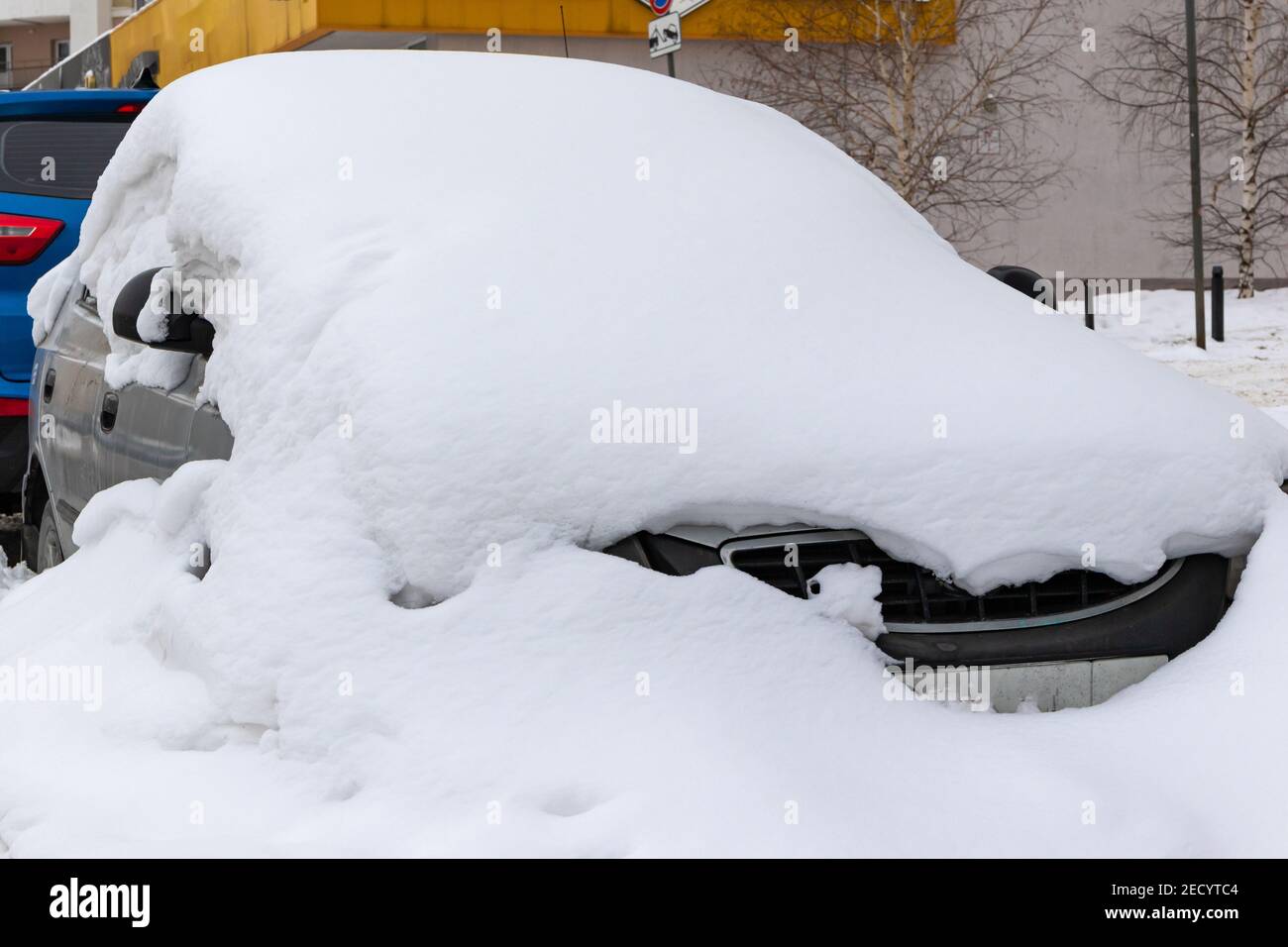 old abandoned broken car parked by the road under a large layer of snow ...