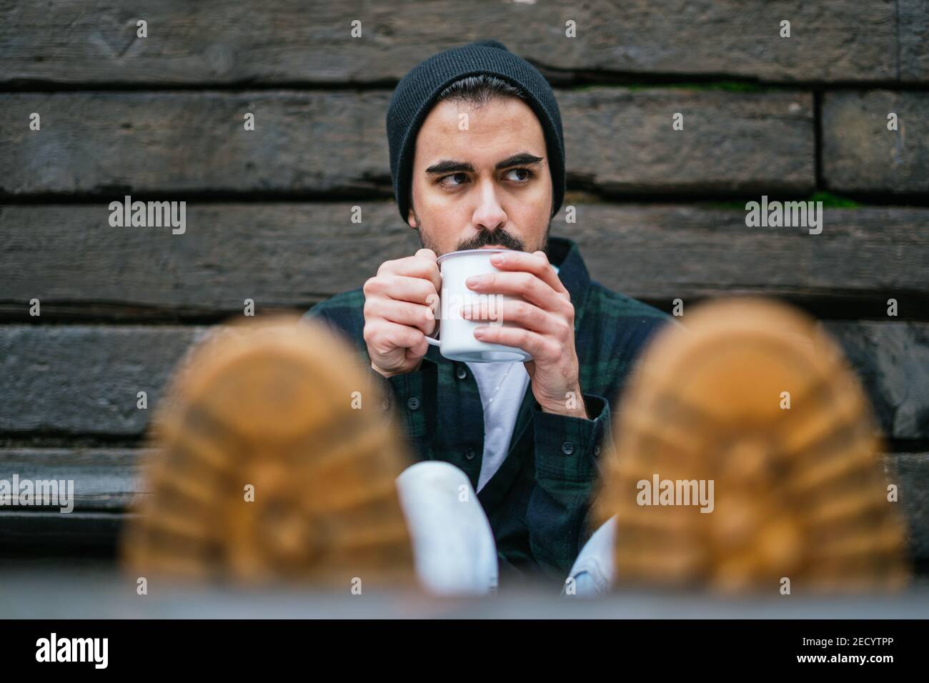 A young brooding hipster wearing a beanie hat is sitting outdoors with ...