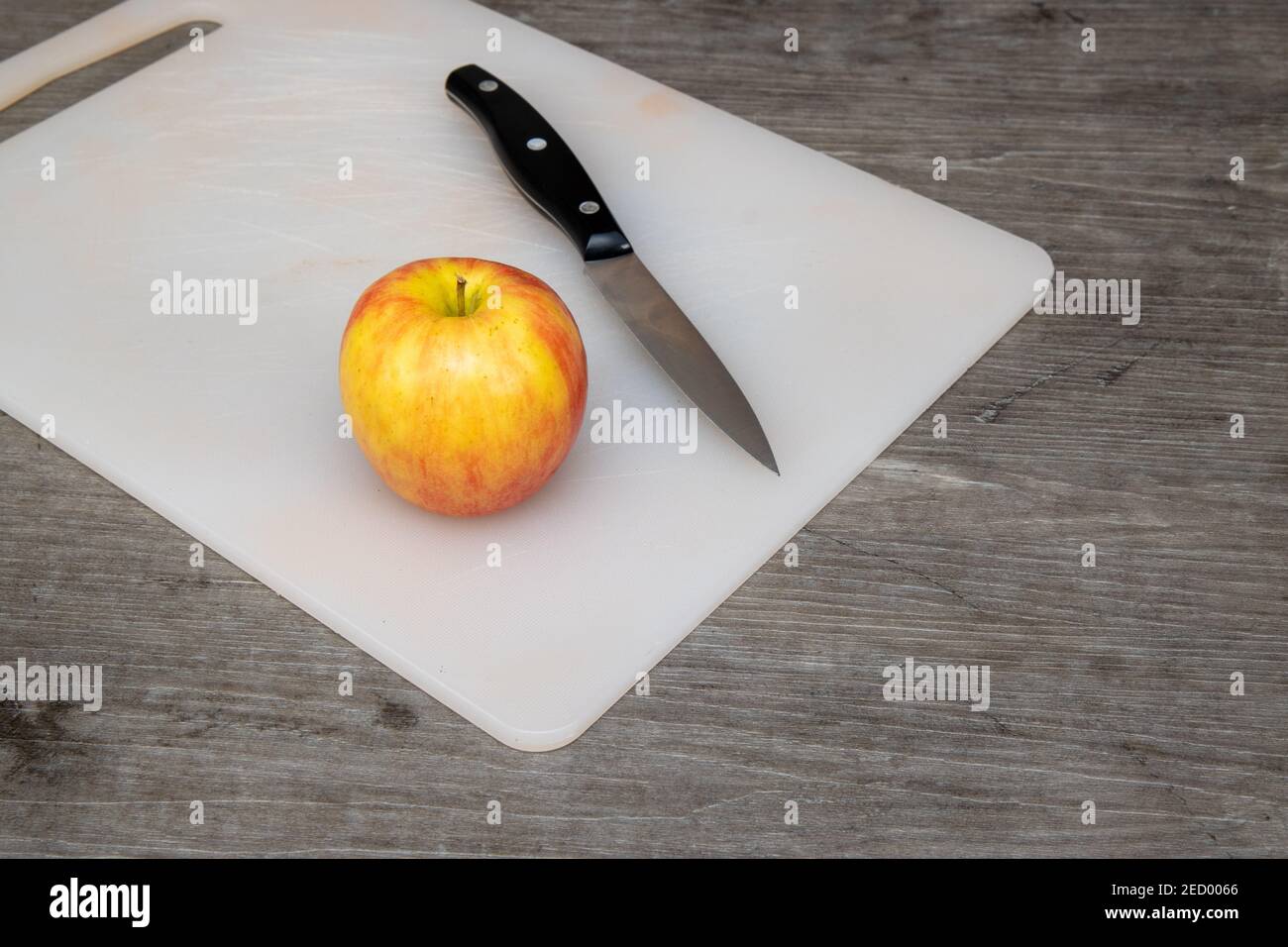 A plastic chopping board in a kitchen with a knife next to an apple ...