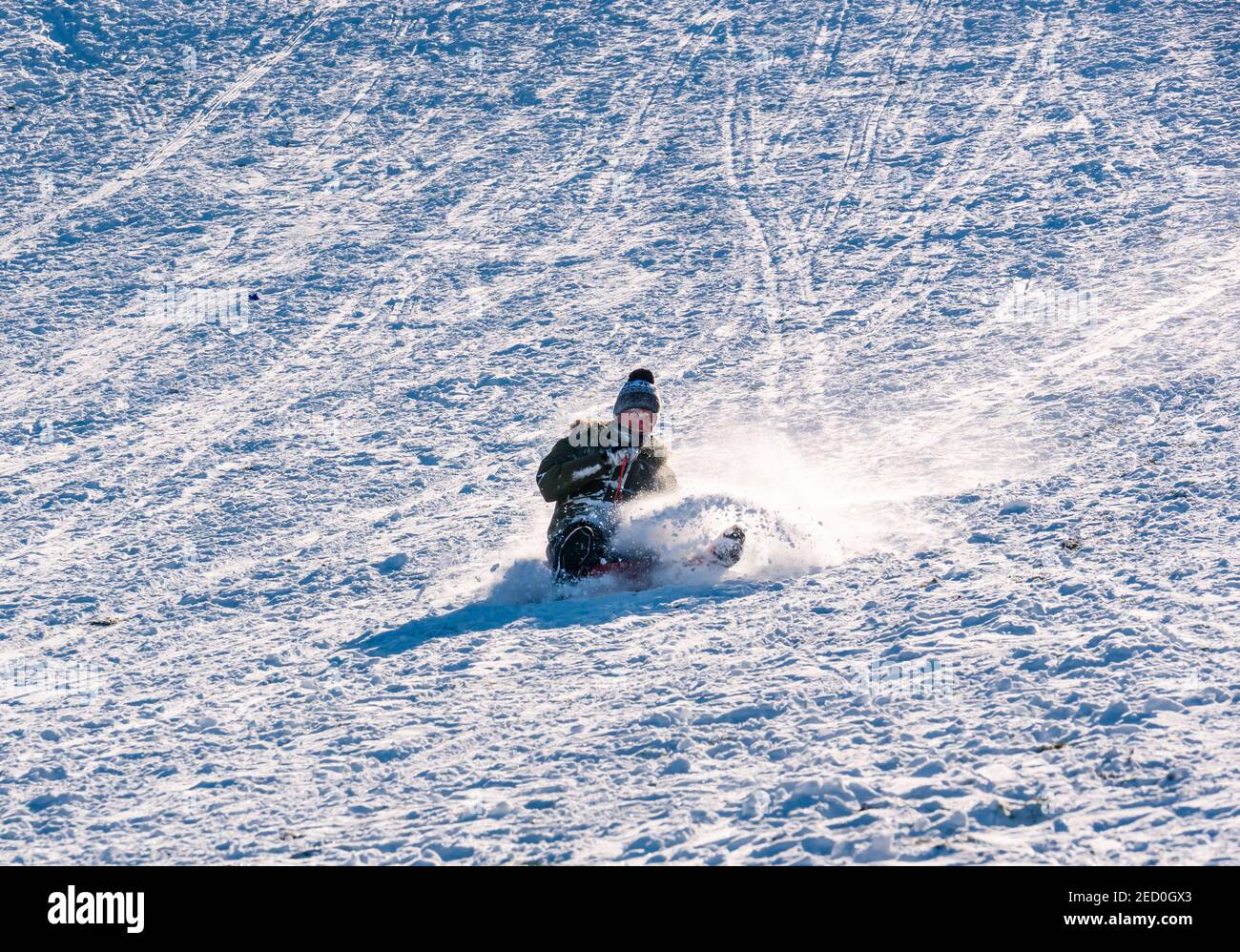 A man slides down a slope on a sledge sledging on Skid Hill in Winter ...