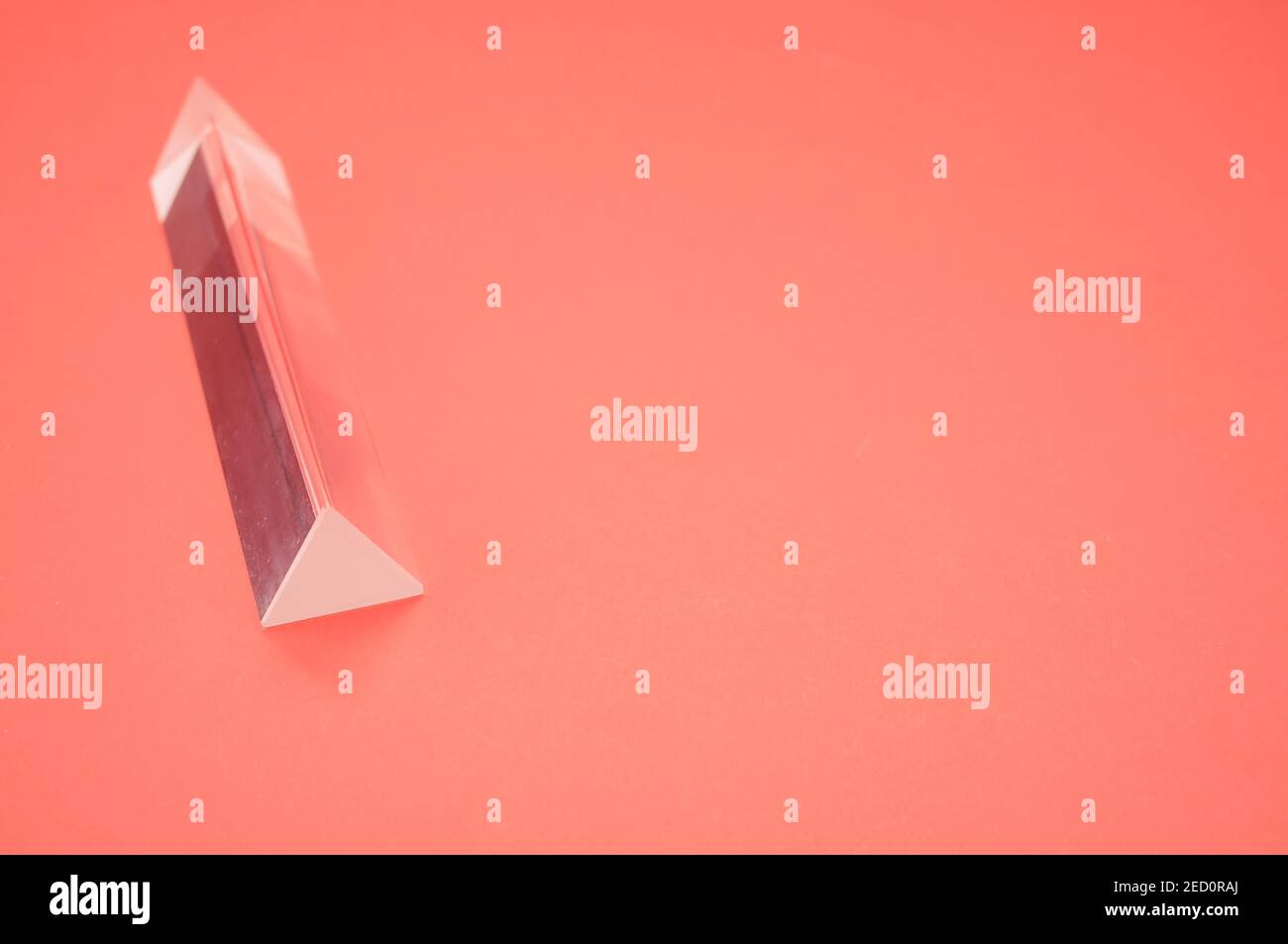 A closeup shot of a triangular glass prism isolated on a red background ...