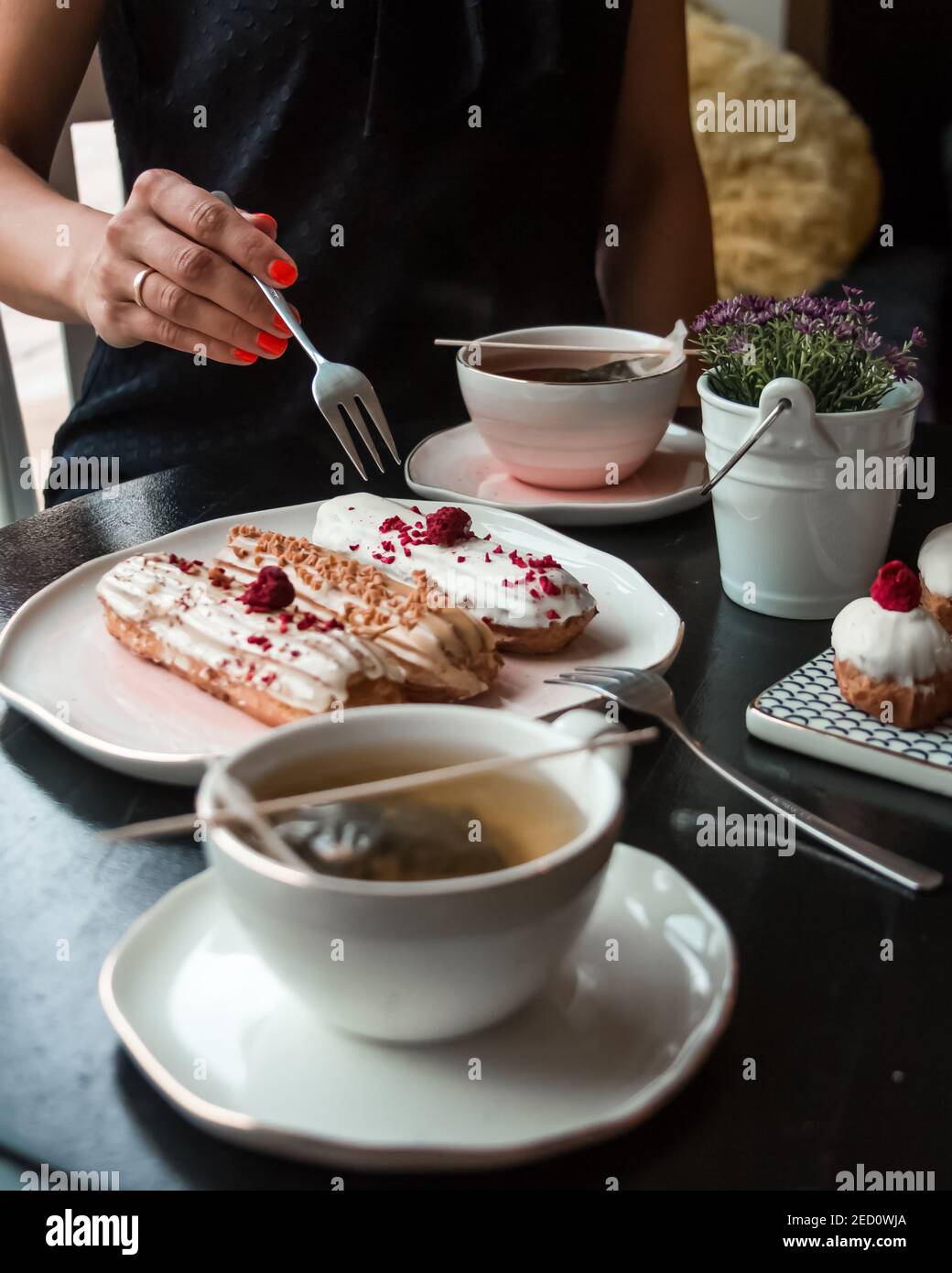A vertical shot of a female eating French eclairs and drinking hot tea ...