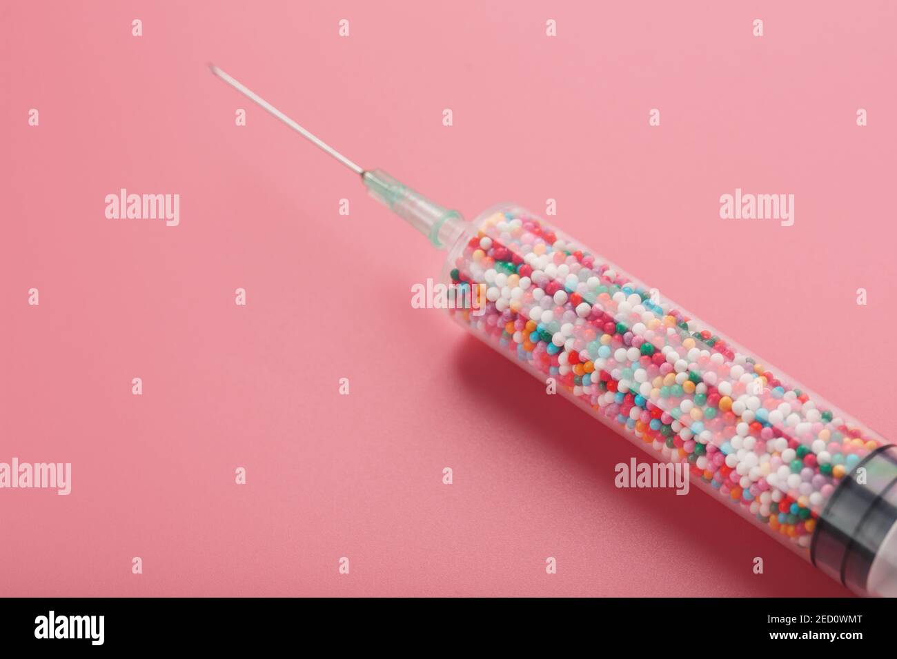 Medical Syringe filled with colorful balloons on a pink background with ...