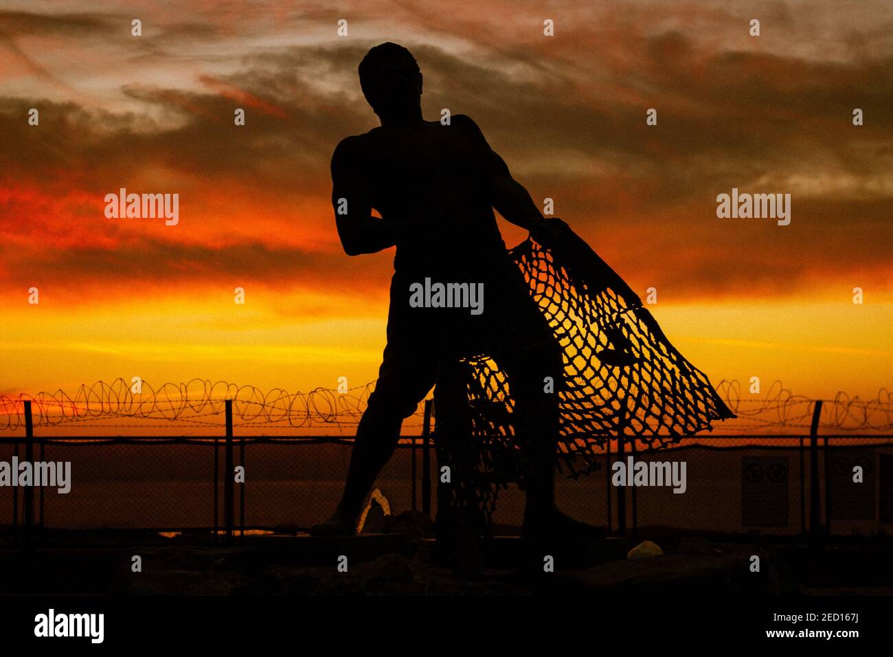 A man statue is hunting the sun with a fishnet during sunset in a ...