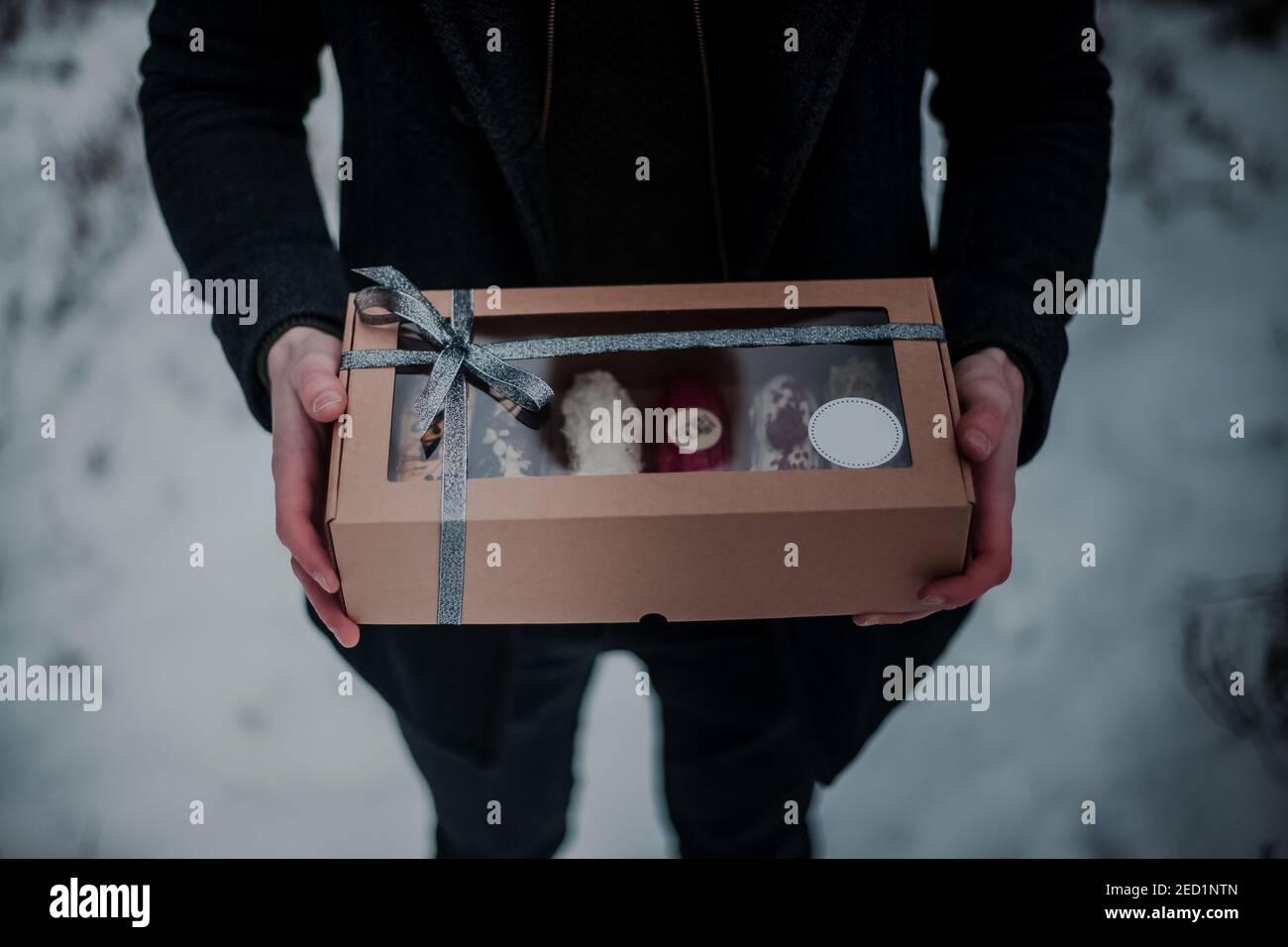 A man in a black coat holding a box with French eclairs Stock Photo - Alamy