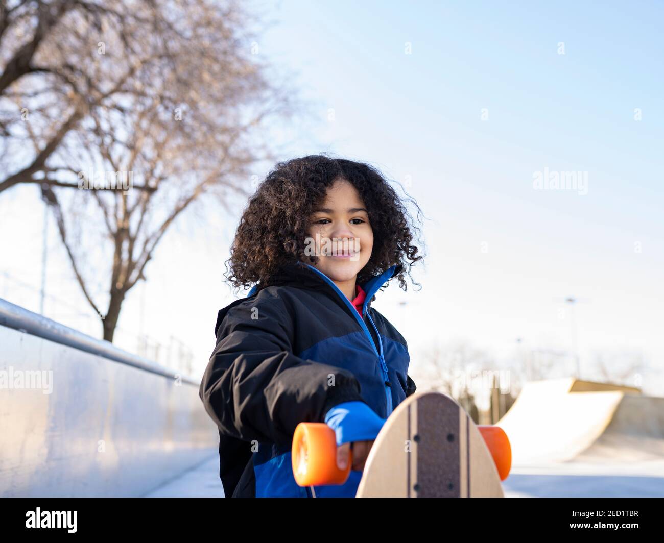 Delighted ethnic child with Afro hairstyle standing with longboard on ...