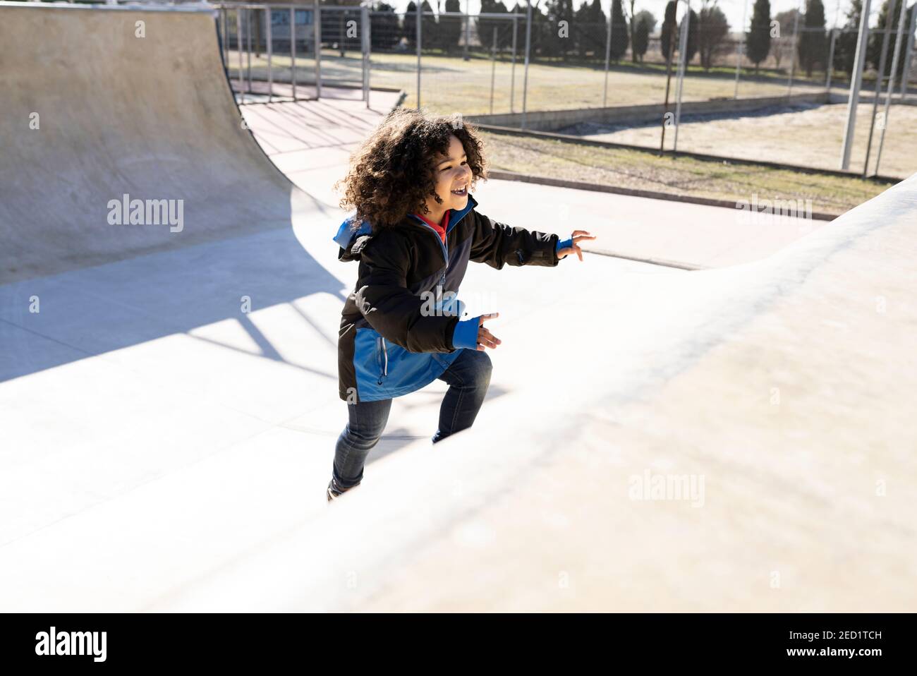 Side view of positive ethnic child with Afro hairstyle running up ramp ...