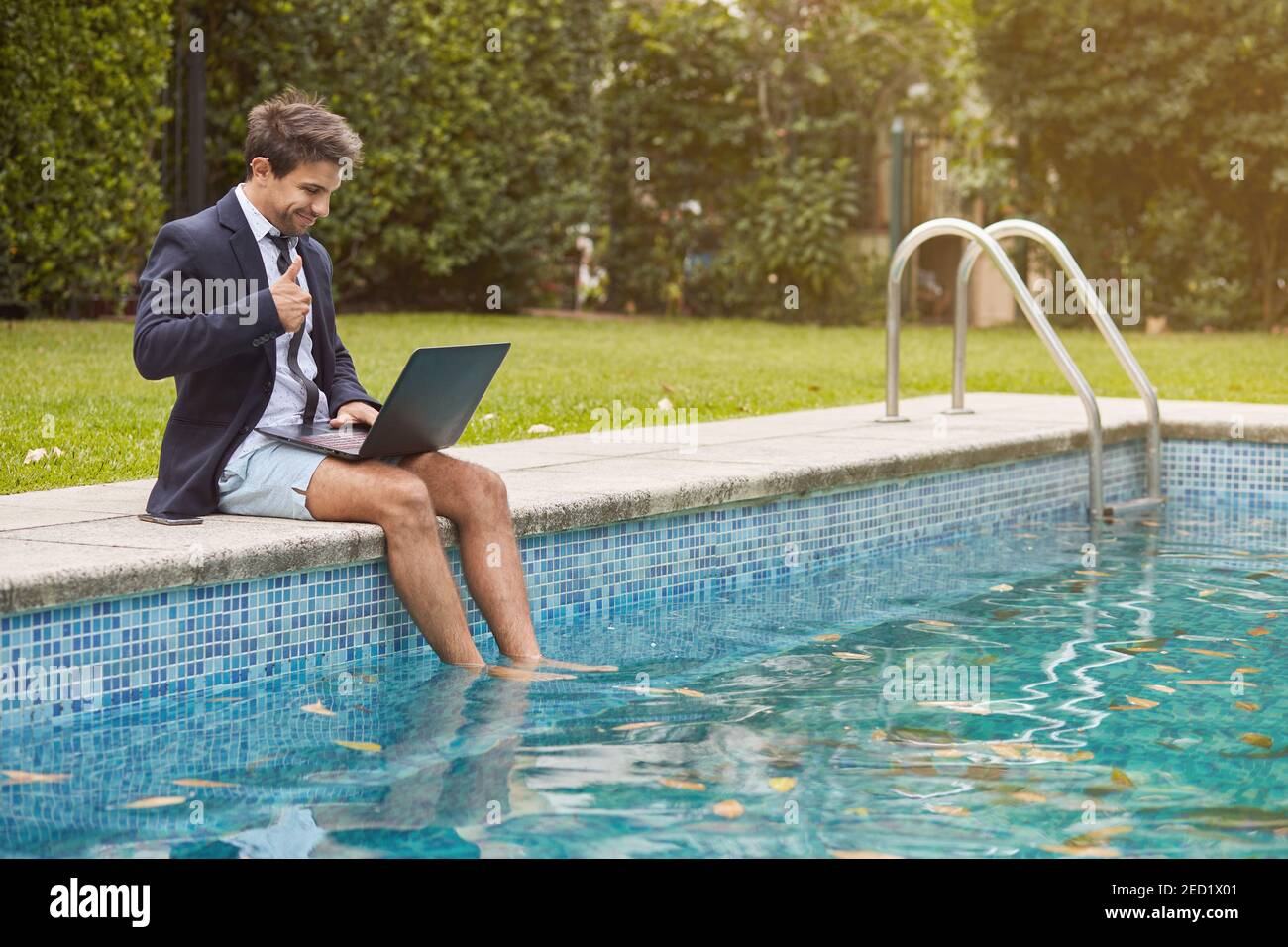 Businessman dressed in a suit sitting on the edge of the pool with a ...