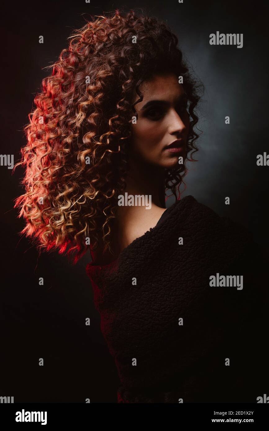 Side view of serene seductive female with curly hair and brown eyes looking at camera on black ...