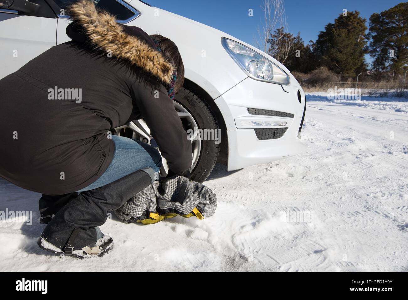 Side view of anonymous female driver changing wheel of car in winter ...