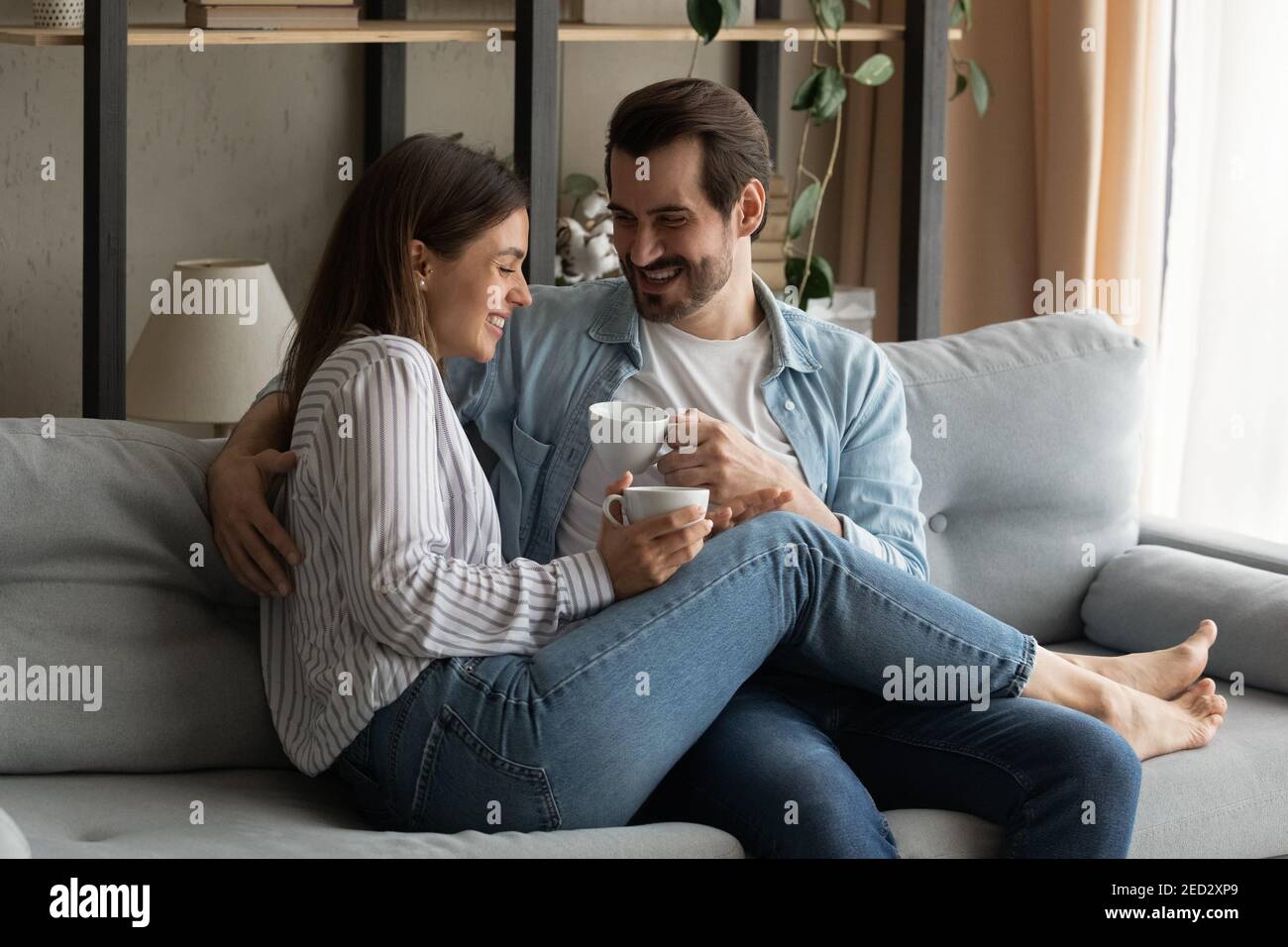 Affectionate young spouses cuddling on couch having pleasure drinking ...