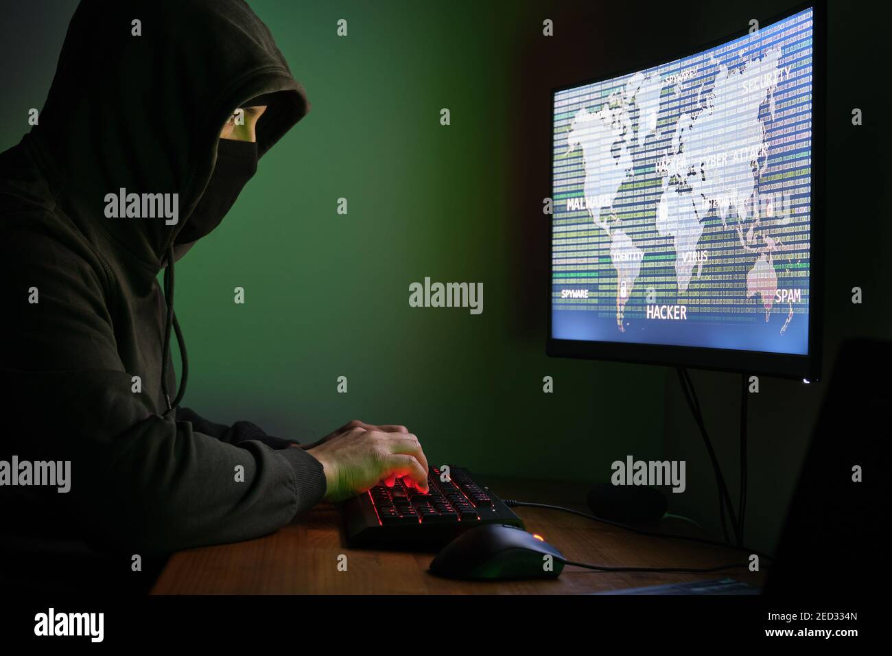 Masked hacker typing in a computer for organizing massive data breach attack around the world ...