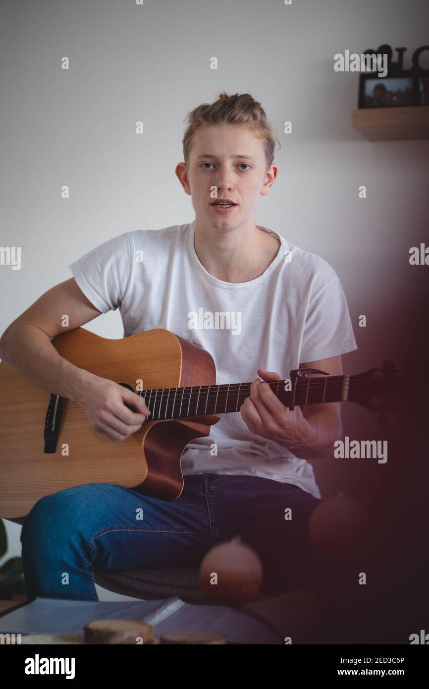 portrait of a blond singer sitting on a low stool strumming a guitar ...