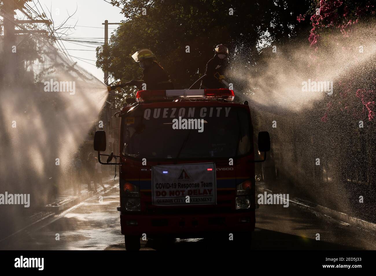 Fireman uses a hoses to spray disinfectant solution along a street to ...