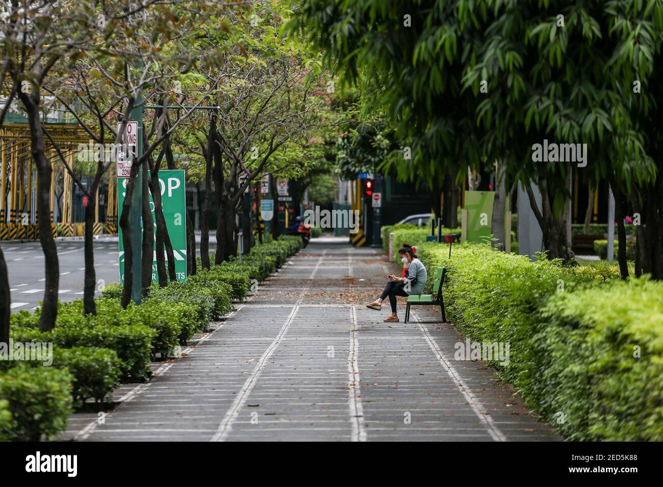 A woman sits alone on a bench along a sidewalk during the coronavirus ...