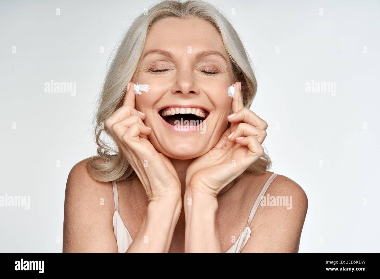 Happy funny 50s middle aged woman applying cream on face isolated on ...