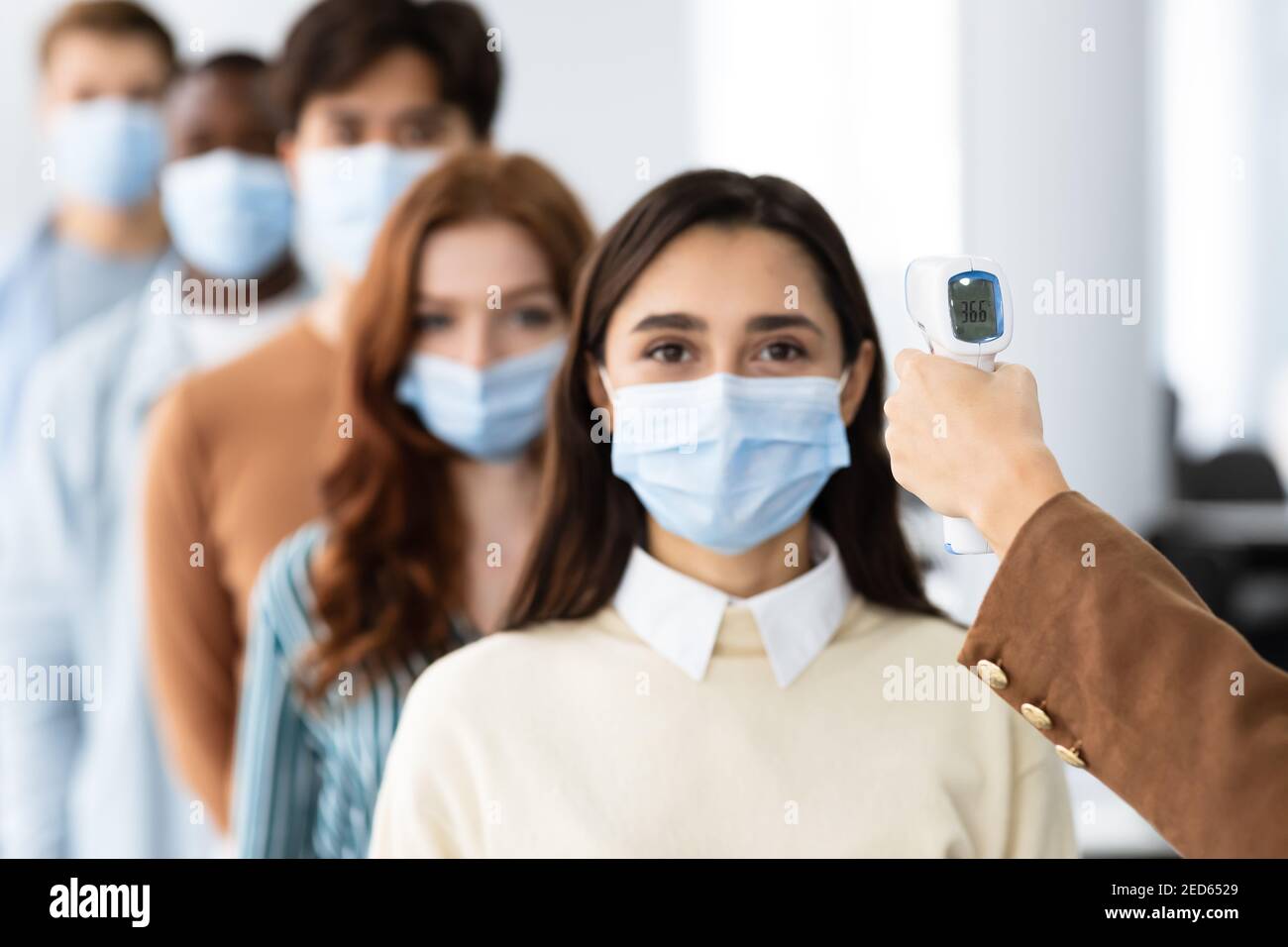 Woman with contactless thermometer screening temperature of multiracial ...
