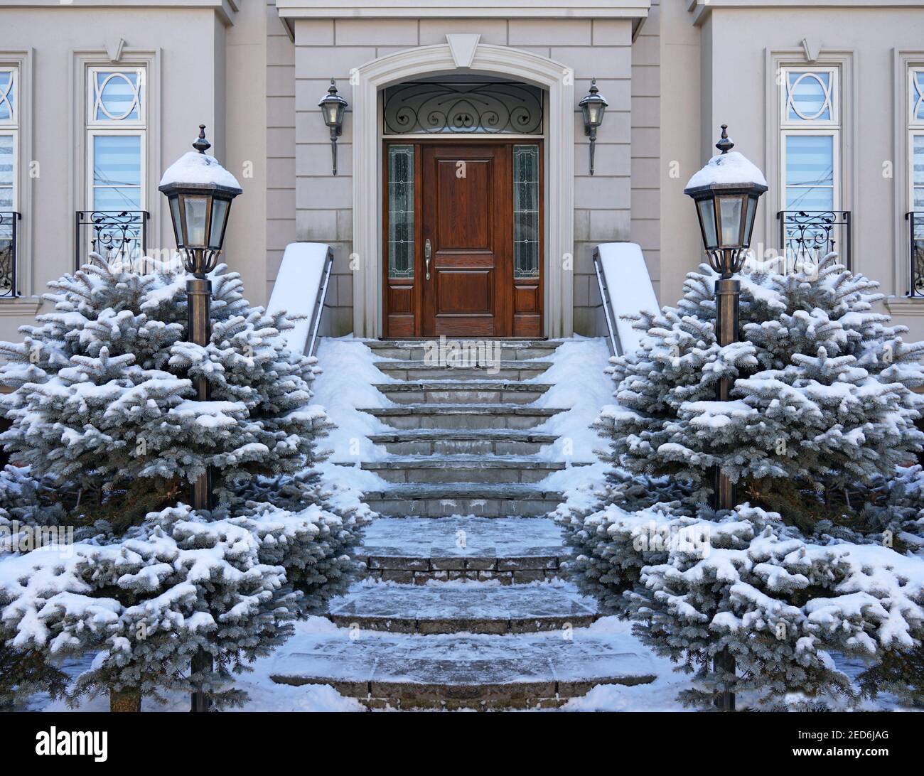 Elegant wood grain front door of house in winter with snow covered pine ...