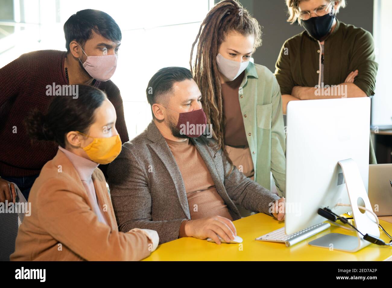 Group of young creative designers gathered by table in front of ...