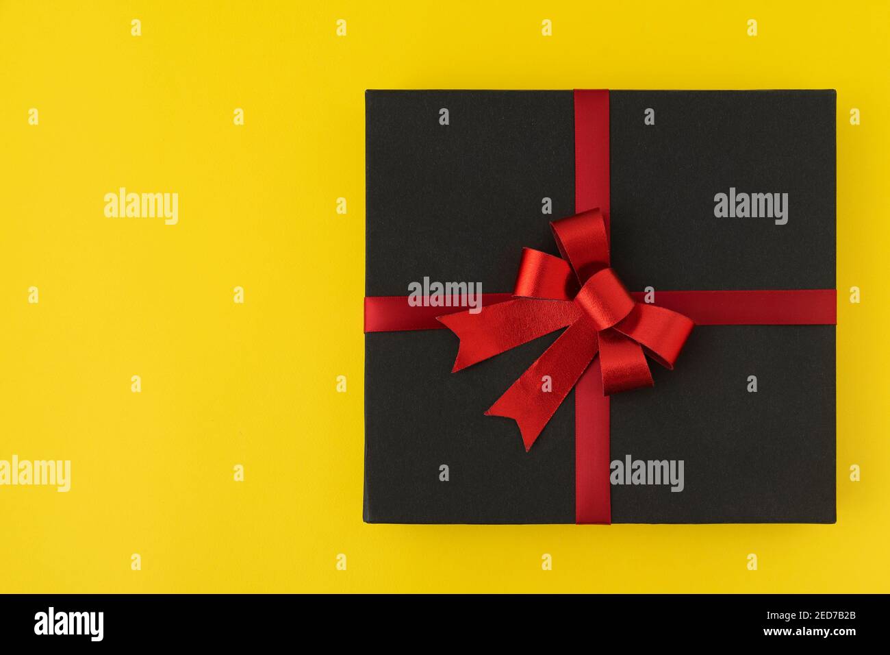 Black box with a red ribbon and a bow on a bright yellow background ...