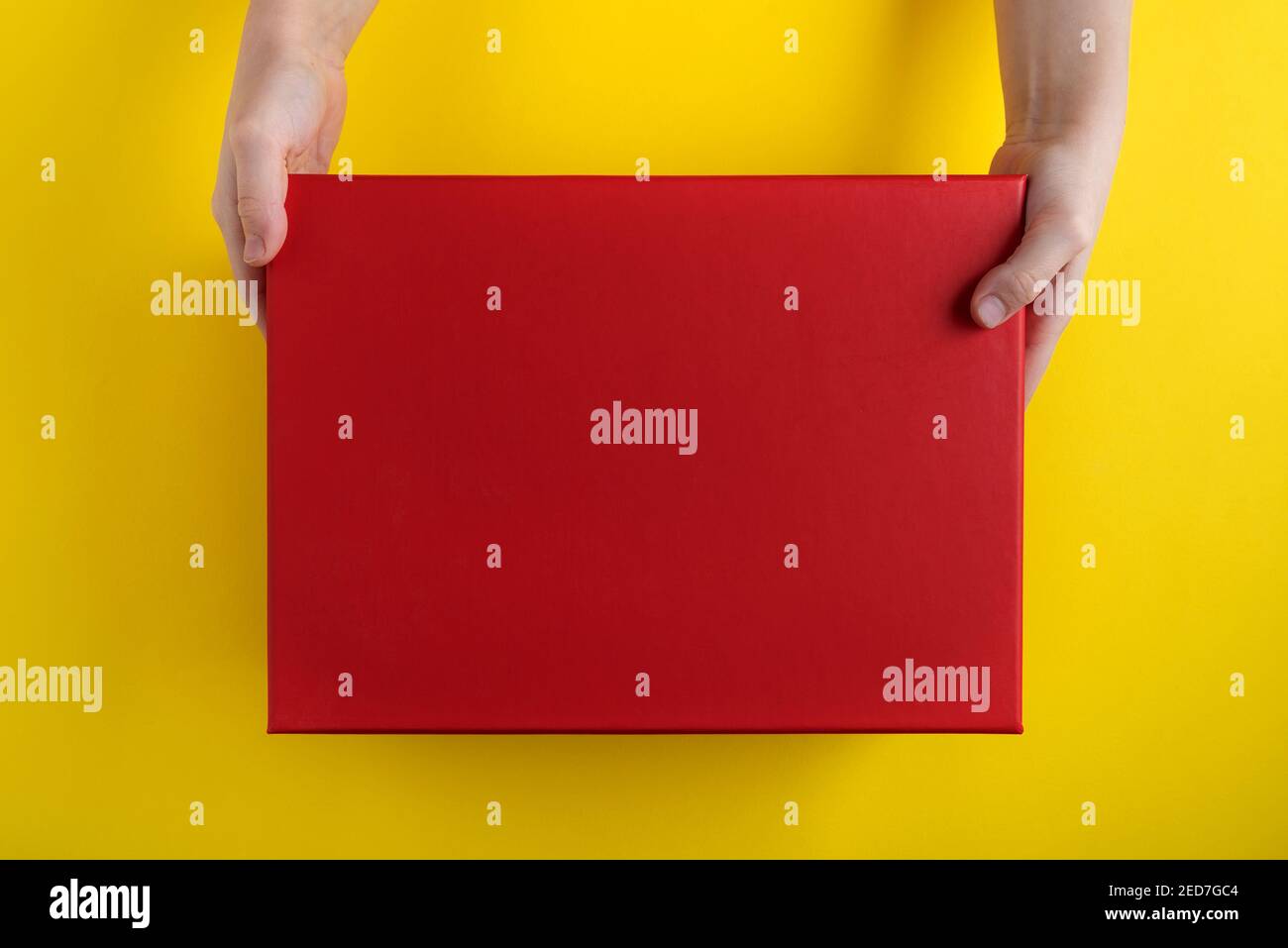 Child hands hold large red box on yellow background. Copy space. Mock ...
