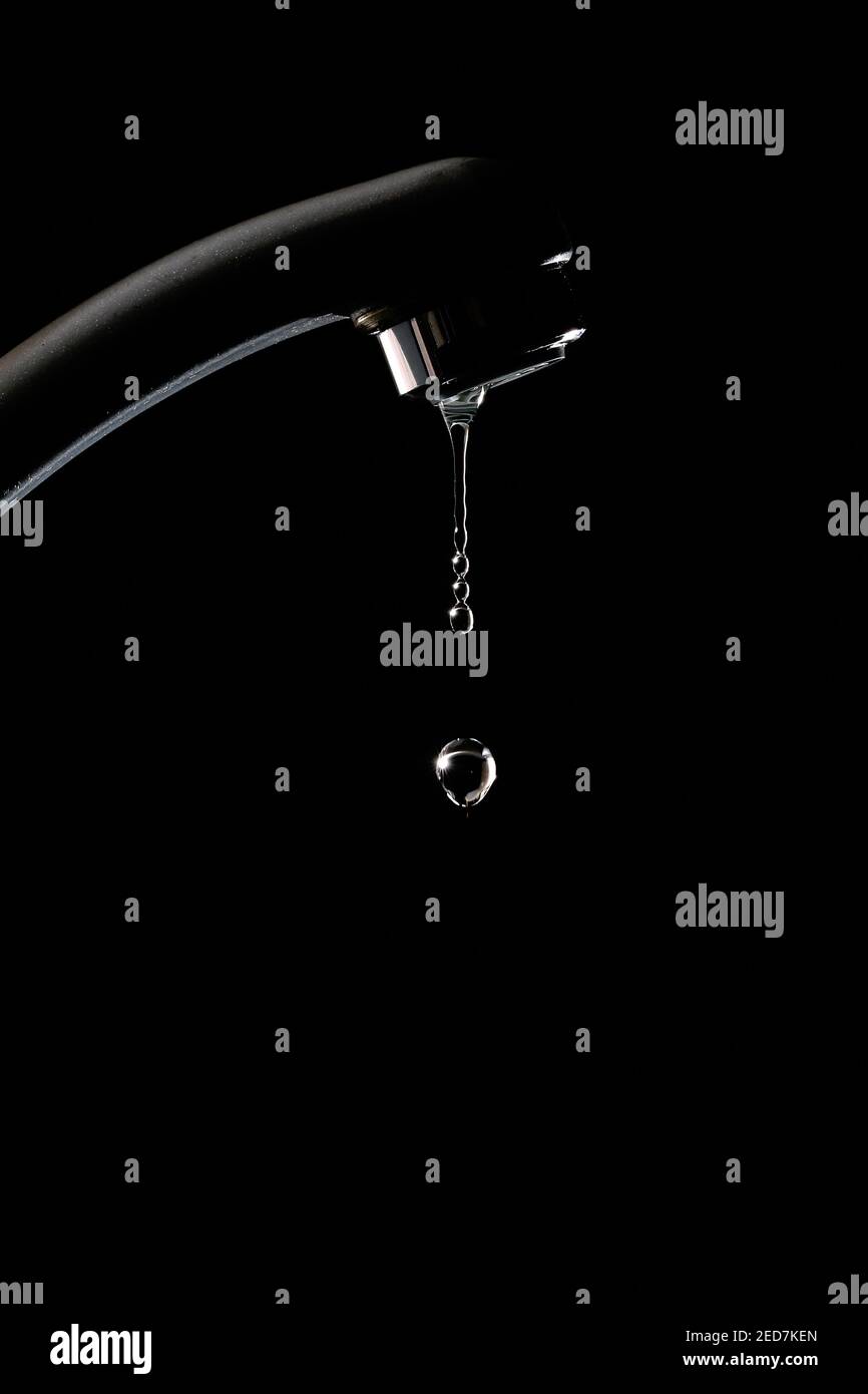 Leaking tap water against a black background, due to the tap being open ...