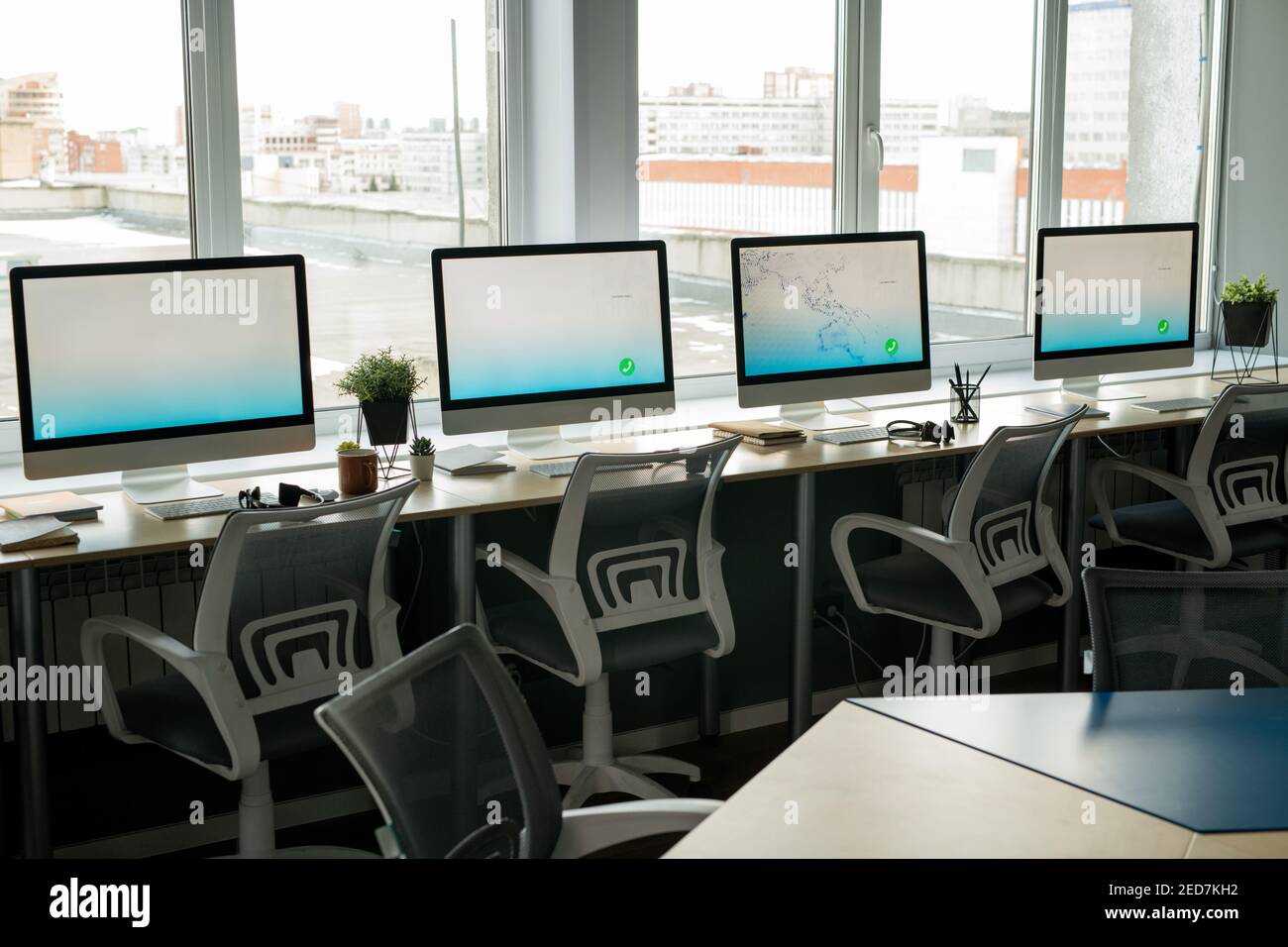 Row of computer monitors standing on desks against large windows inside ...