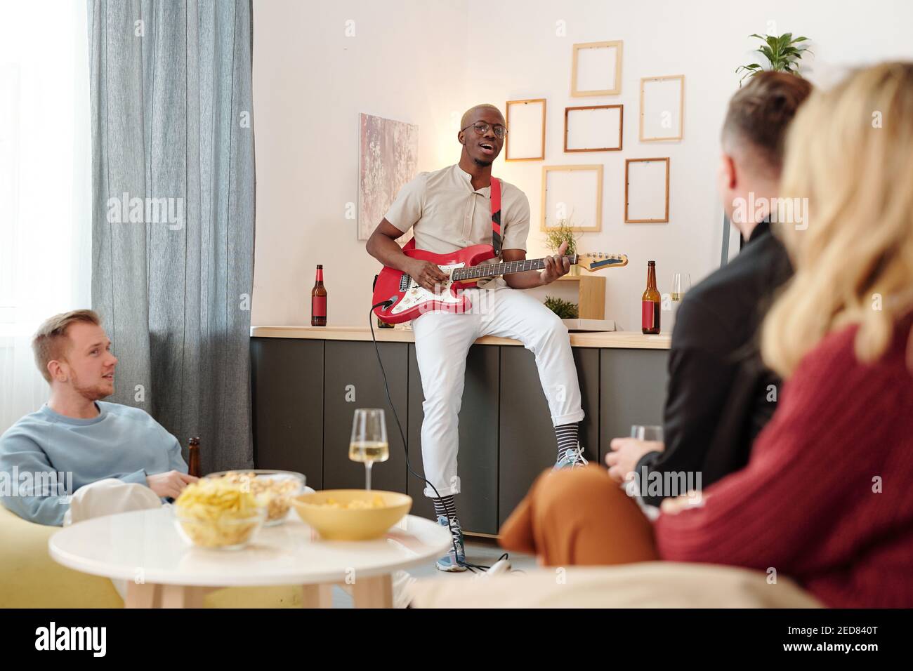 Group of young intercultural friends sitting by small table with snacks ...