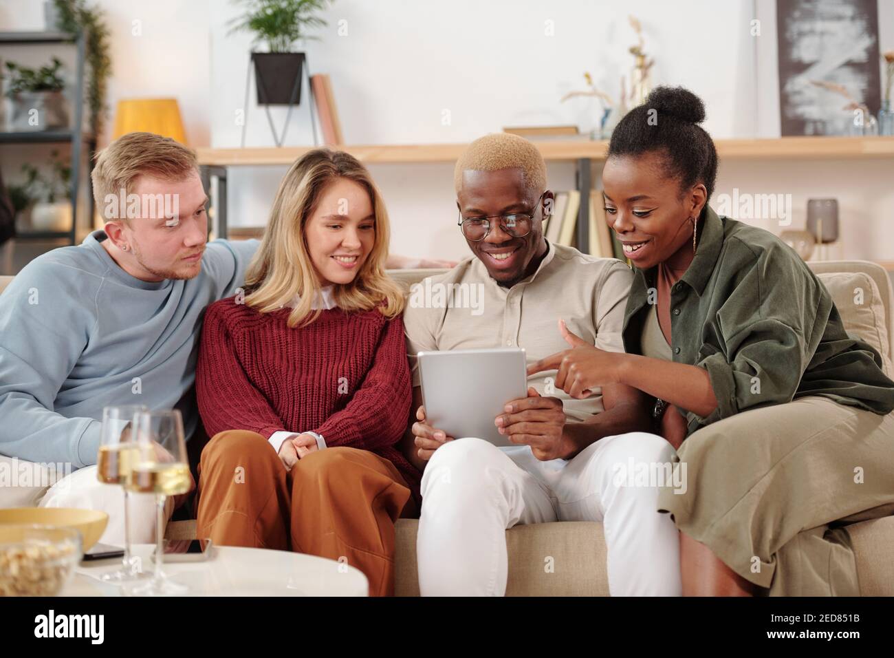 Group of young cheerful intercultural friends sitting in row on couch ...