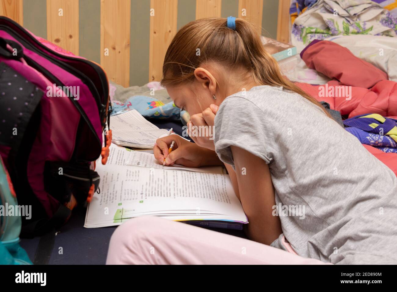 Schoolgirl does her homework on a spread out couch piled high with ...
