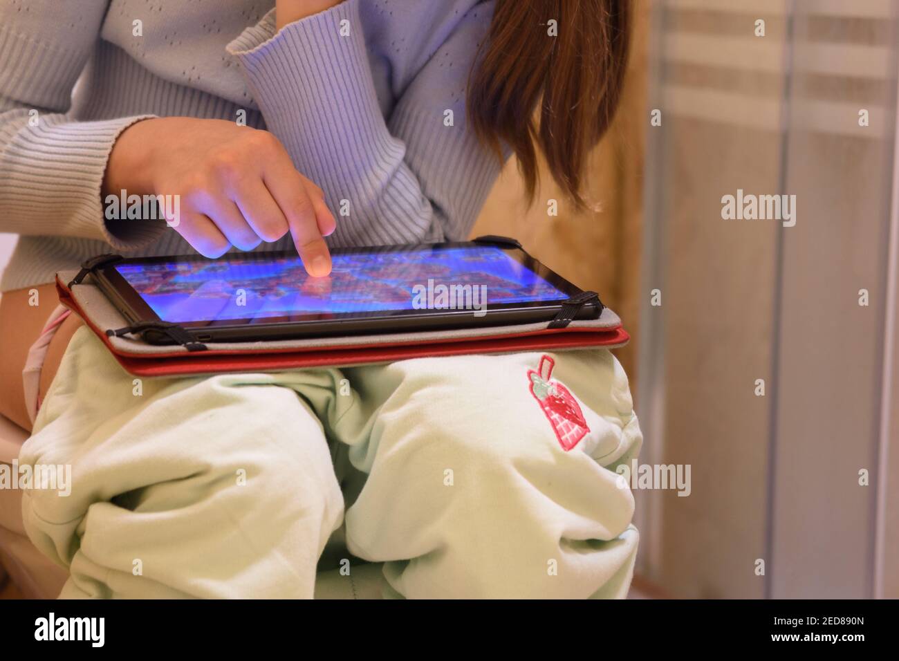 Child sitting on the toilet plays an online game on a tablet computer ...