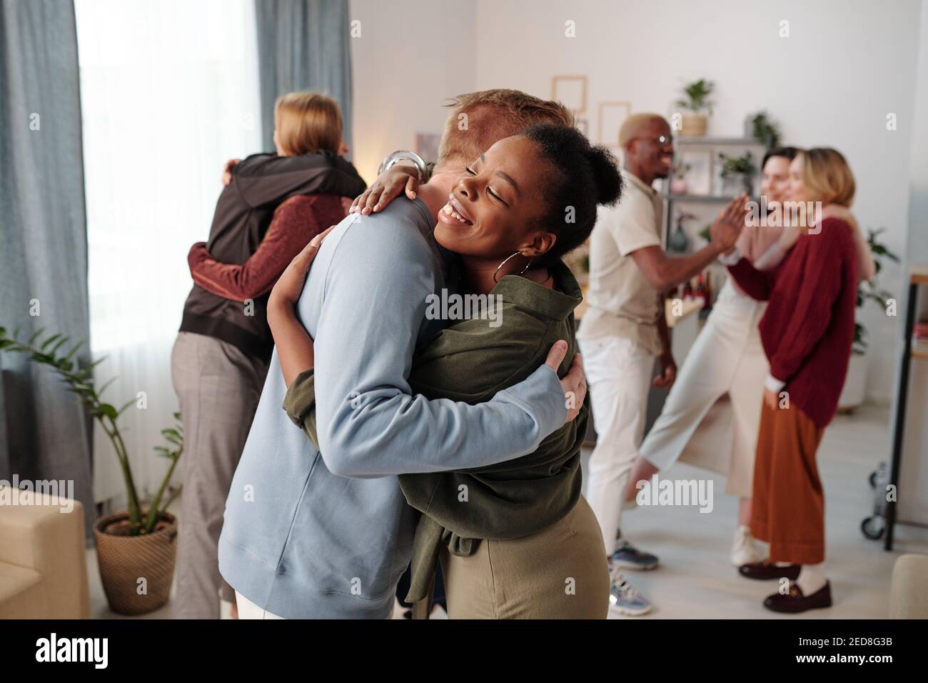 Happy young African woman in smart casualwear giving hug to guy in blue ...