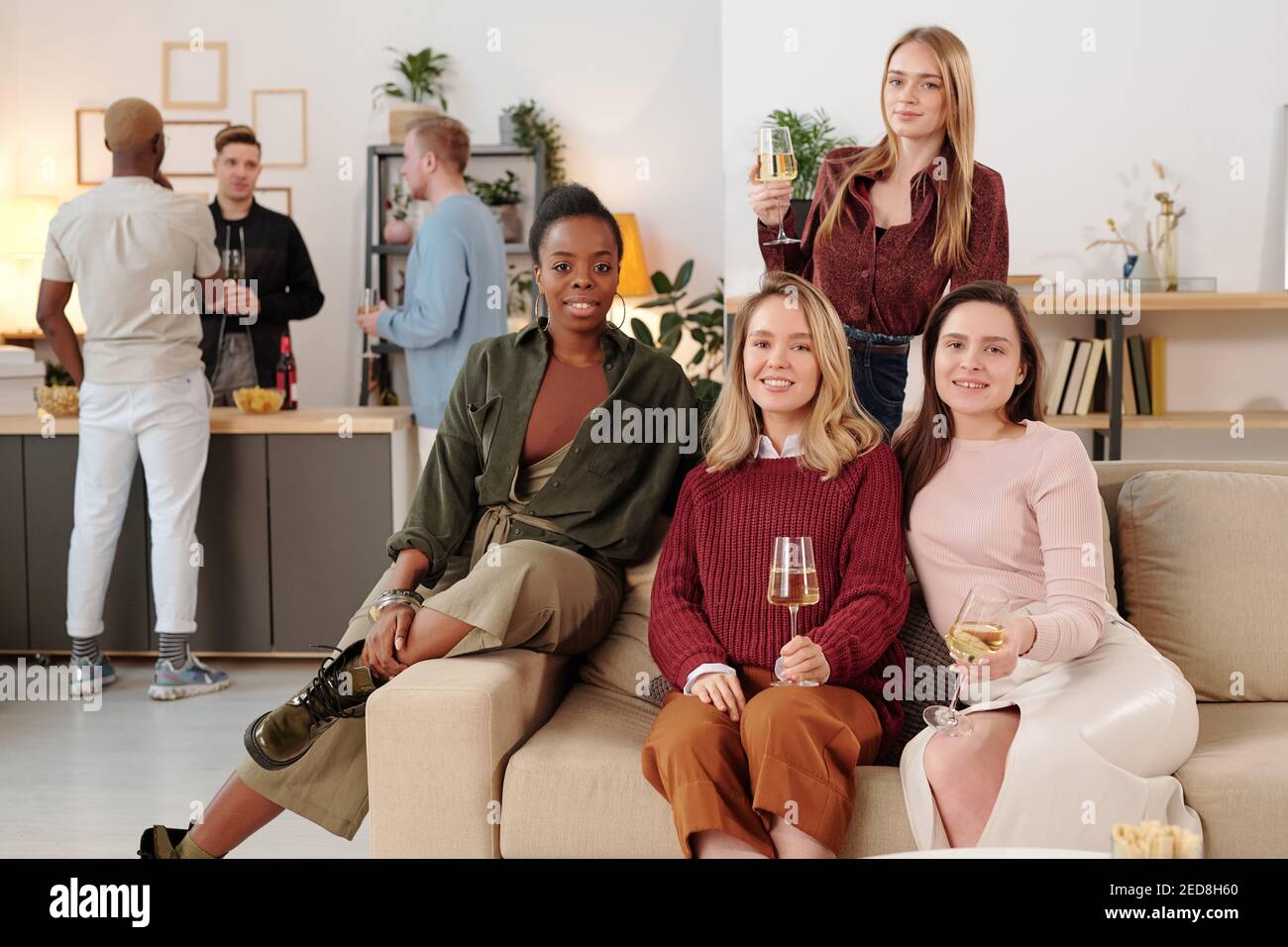 Happy young intercultural women with flutes of champagne looking at you ...