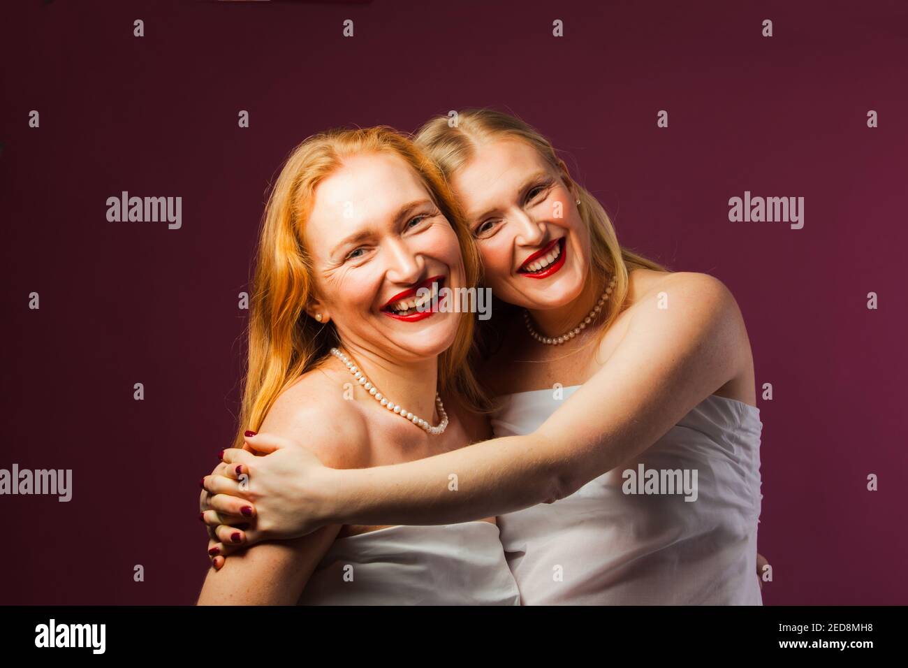 Two pretty sisters hugging on purple background Stock Photo - Alamy