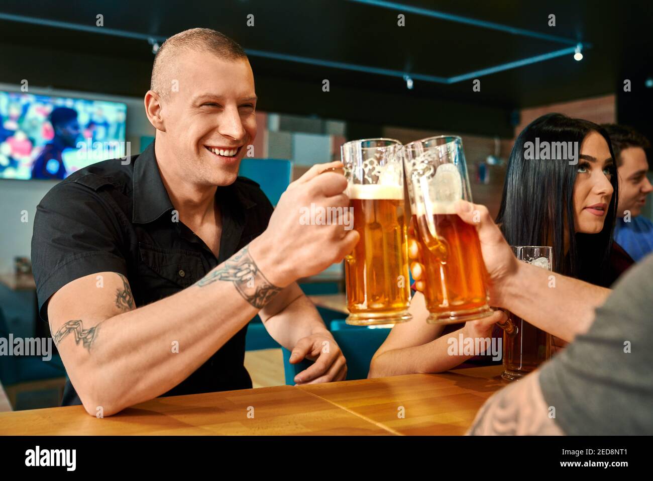 Happy man in black shirt sitting at table and toasting with beer with ...