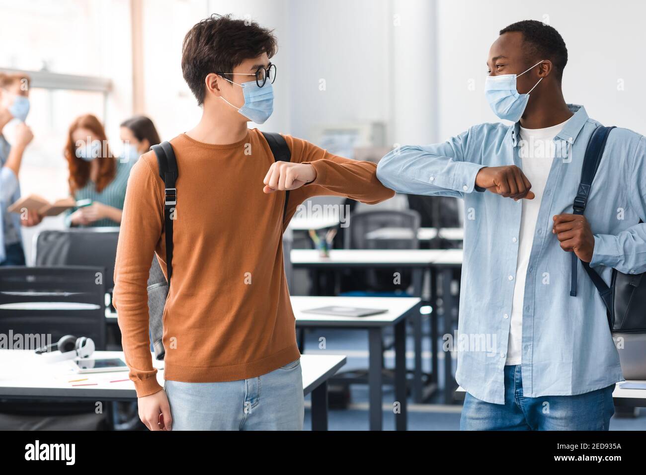 Diverse students wearing face masks greeting and bumping elbows Stock ...