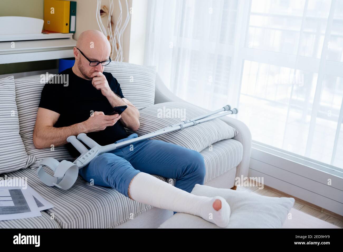 A man with glasses with a broken leg is sitting on the couch at home ...