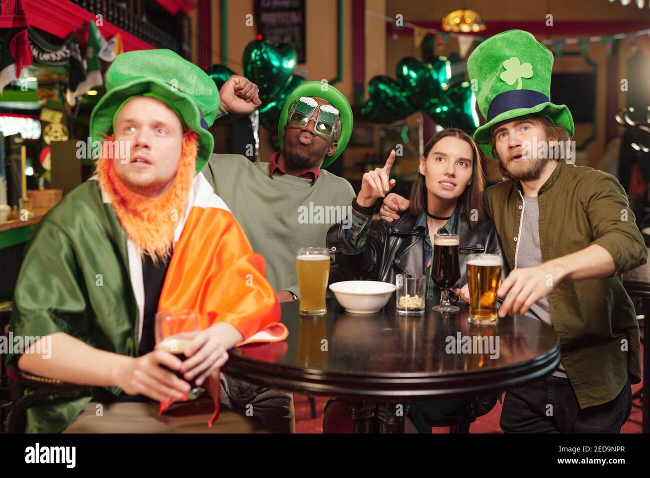 Group of young intercultural football fans in green hats and casualwear ...