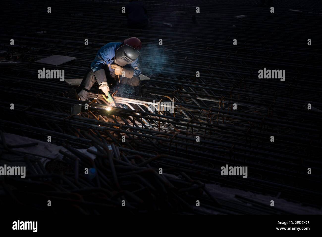A worker using a welding torch fixes parts of a steel mesh for use in ...