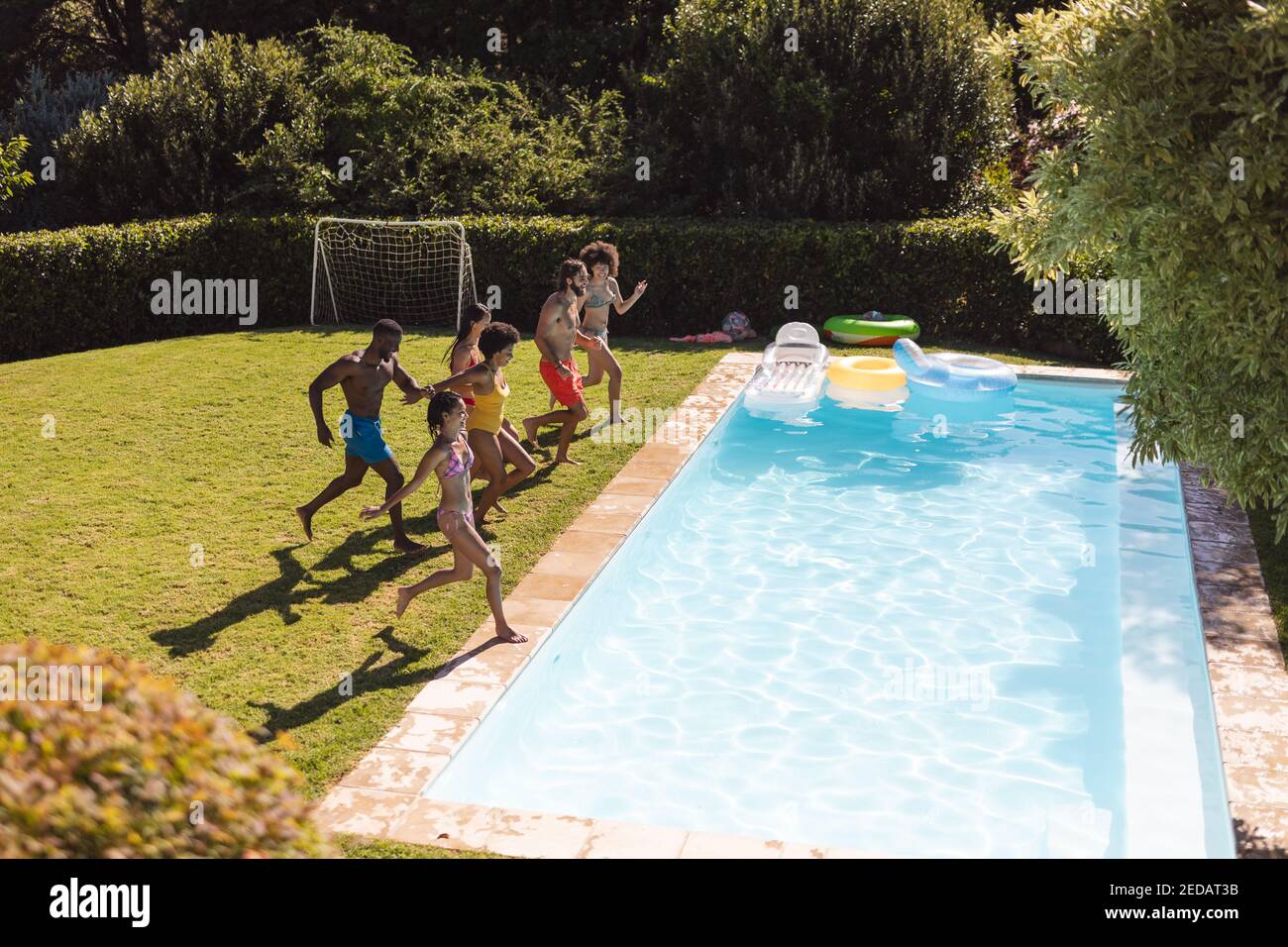 Diverse group of friends having fun and jumping into water at a pool ...