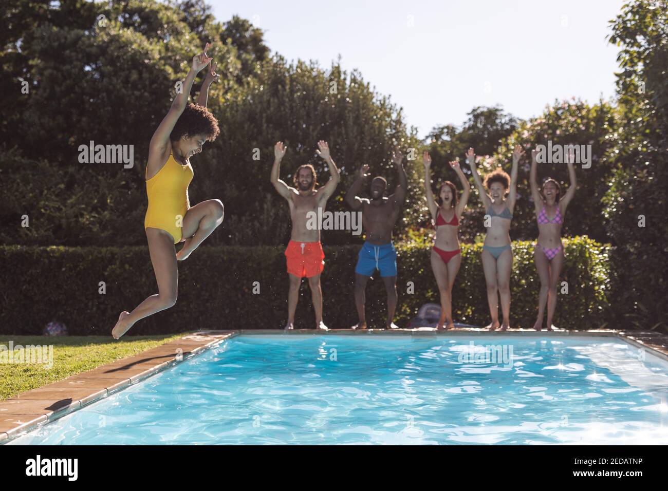 Diverse group of friends having fun and jumping into water at a pool ...