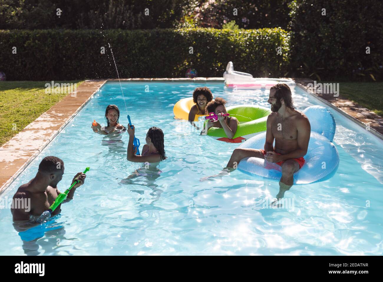 Diverse group of friends having fun playing on inflatables in swimming ...