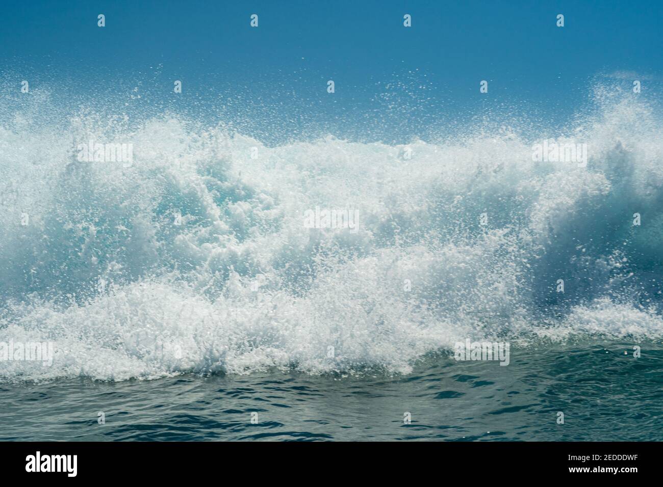 Tumbling white foamy water on a breaking turquoise wave with blue sky ...