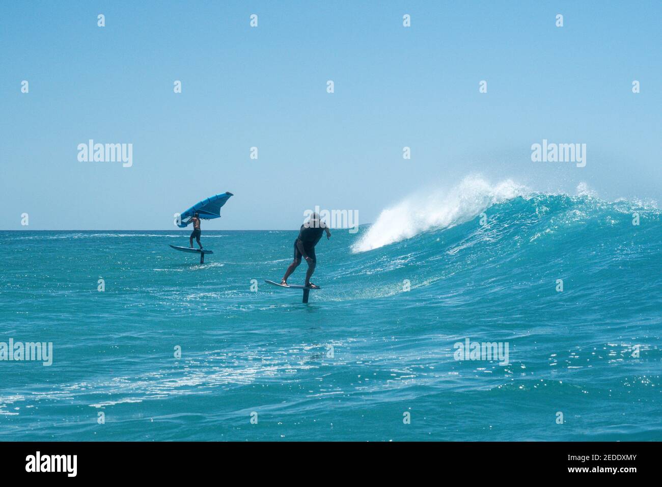 Two men surf a wave using hydrofoil surfboards, one man riding using a ...