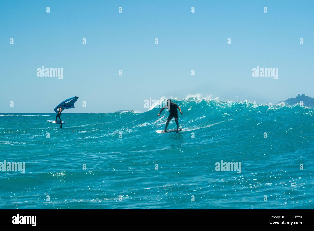 Two men surf a wave using hydrofoil surfboards, one man riding using a ...