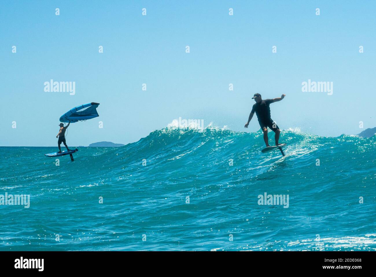 Two men surf a wave using hydrofoil surfboards, one man riding using a ...