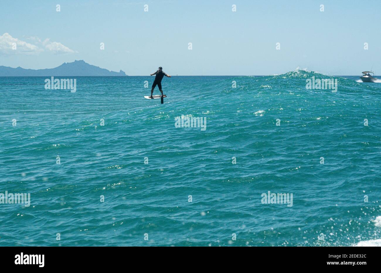 A man surfs on a hydrofoil surfboard on turquoise waves at Mangawhai ...
