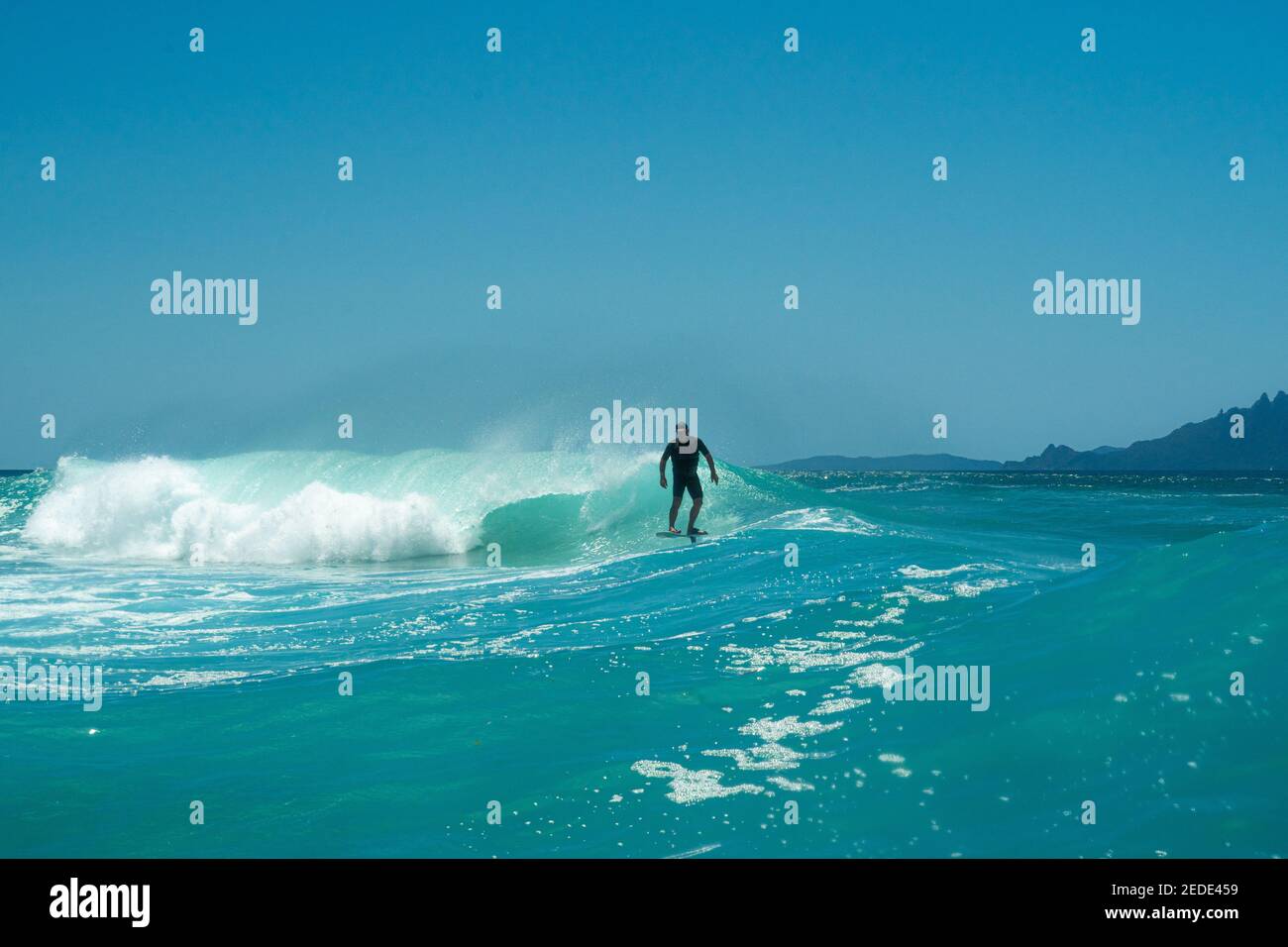 A man surfs on a hydrofoil surfboard on turquoise waves at Mangawhai ...