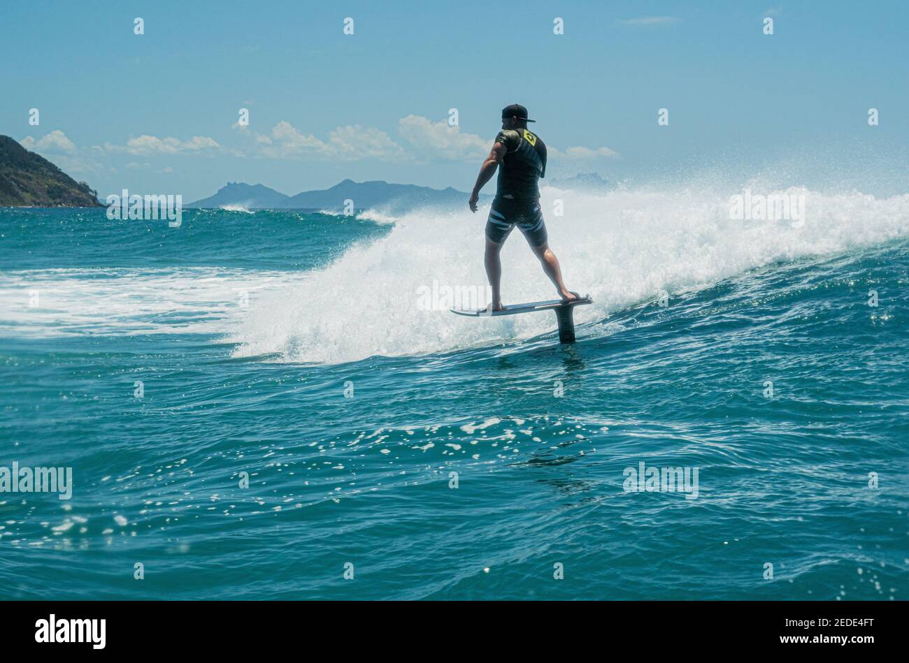A man surfs on a hydrofoil surfboard on turquoise waves at Mangawhai ...